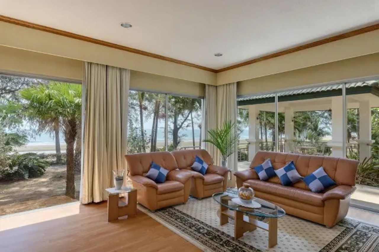 Uma sala de estar ampla com uma grande janela com vista para a praia, mobiliada com sofás de couro e uma mesa de centro.