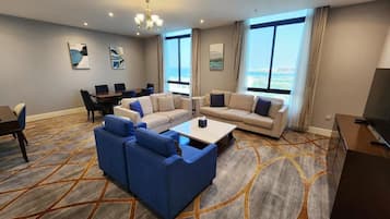 Quarto de hotel com área de estar, mesa de jantar e grandes janelas.