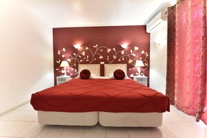 Uma cama de casal com colcha vermelha, duas luminárias de cabeceira e um desenho floral na parede.