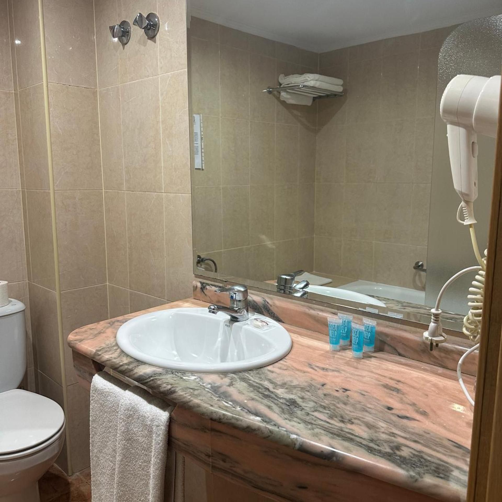 Casa de banho com lavatório de mármore, toalha pendurada na parede, secador de cabelo e espelho.