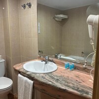 Casa de banho com lavatório de mármore, toalha pendurada na parede, secador de cabelo e espelho.