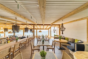 Um espaço amplo para bar, com vigas de madeira, assentos e vista para o mar.
