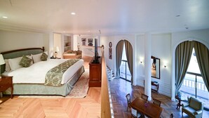 Um quarto de hotel espaçoso com uma cama grande, um espaço de estar com mesa e cadeiras, e uma varanda com vista.