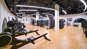 Uma academia com diversos equipamentos de exercícios, incluindo esteiras e aparelhos de musculação, dispostos em um espaço amplo com piso de madeira e iluminação moderna.