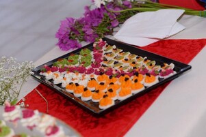Uma bandeja com sushi colorido disposto sobre um prato preto, acompanhado por flores roxas e um pano vermelho.