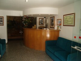 Uma área de recepção com um balcão de madeira, um sofá azul e uma escada que leva a um andar superior.