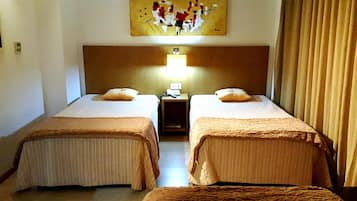 Quarto de hotel com duas camas, uma mesinha de cabeceira, um abajur e um quadro na parede.