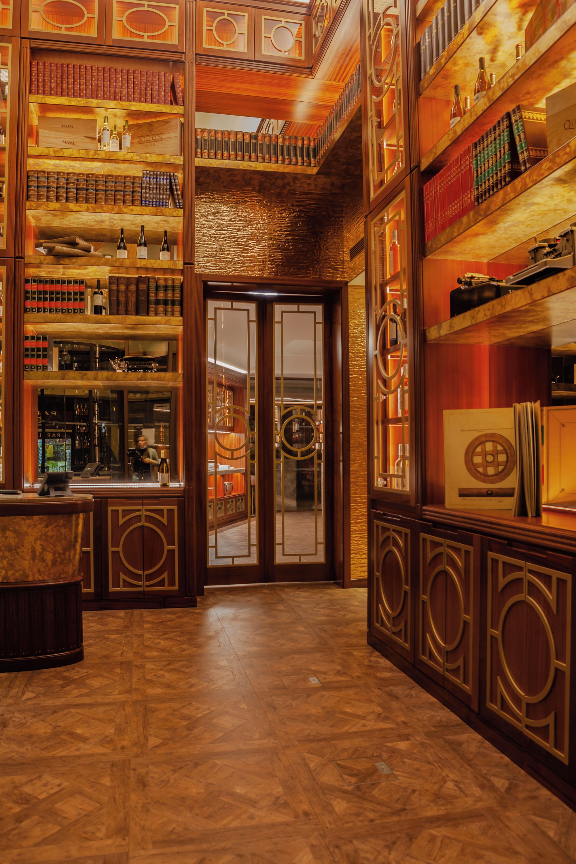 Um hall amplo com piso de madeira, um balcão de recepção e uma grande porta de vidro que dá para um espaço de bar.