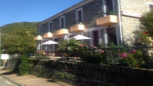 Um edifício de dois andares com varandas, uma placa indicando que é um hotel e um muro de pedra com plantas floridas na frente.