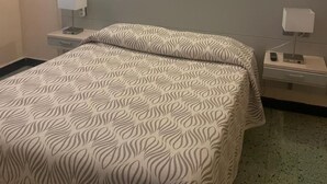 Quarto de hotel com cama, mesa de cabeceira, luminária na parede e uma pequena mesa.