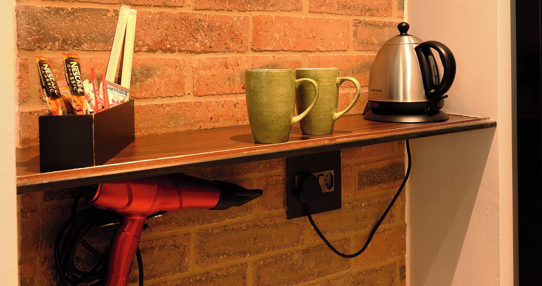 Uma bancada de cozinha com uma cafeteira, duas canecas e uma caixa de utensílios.