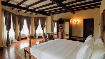 Quarto de hotel com uma cama grande, piso de madeira e teto com vigas aparentes.