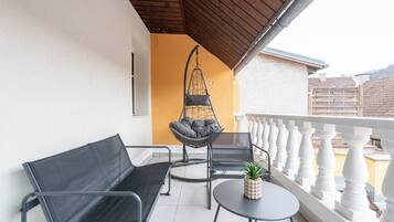 Varanda com sofá preto, cadeira suspensa e pequena mesa com uma planta.