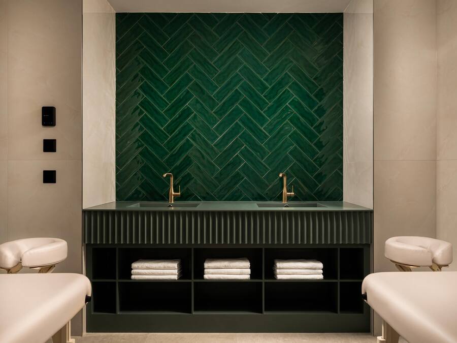 Uma casa de banho moderna com duas lavatórios, parede com padrão herringbone e um porta-toalhas.