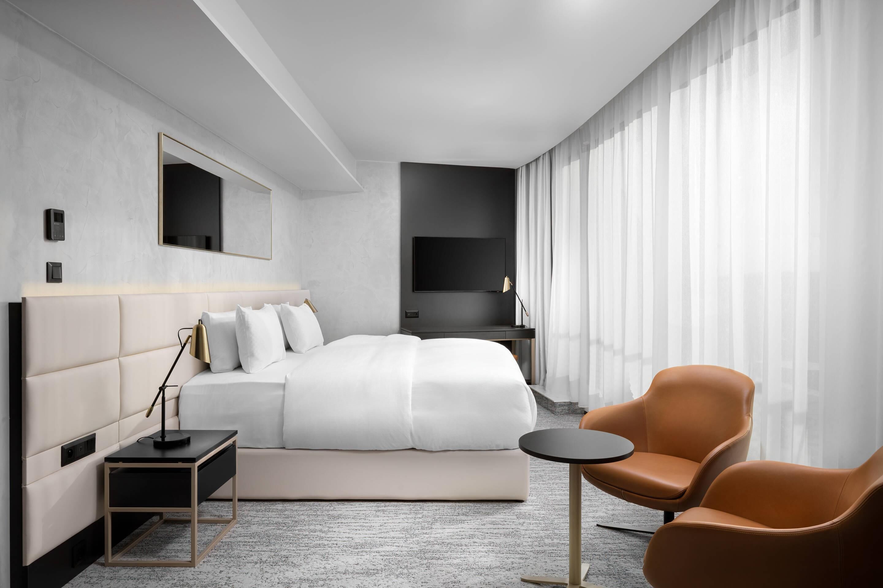 Quarto de hotel moderno com uma cama grande, televisão, escrivaninha e uma cadeira.