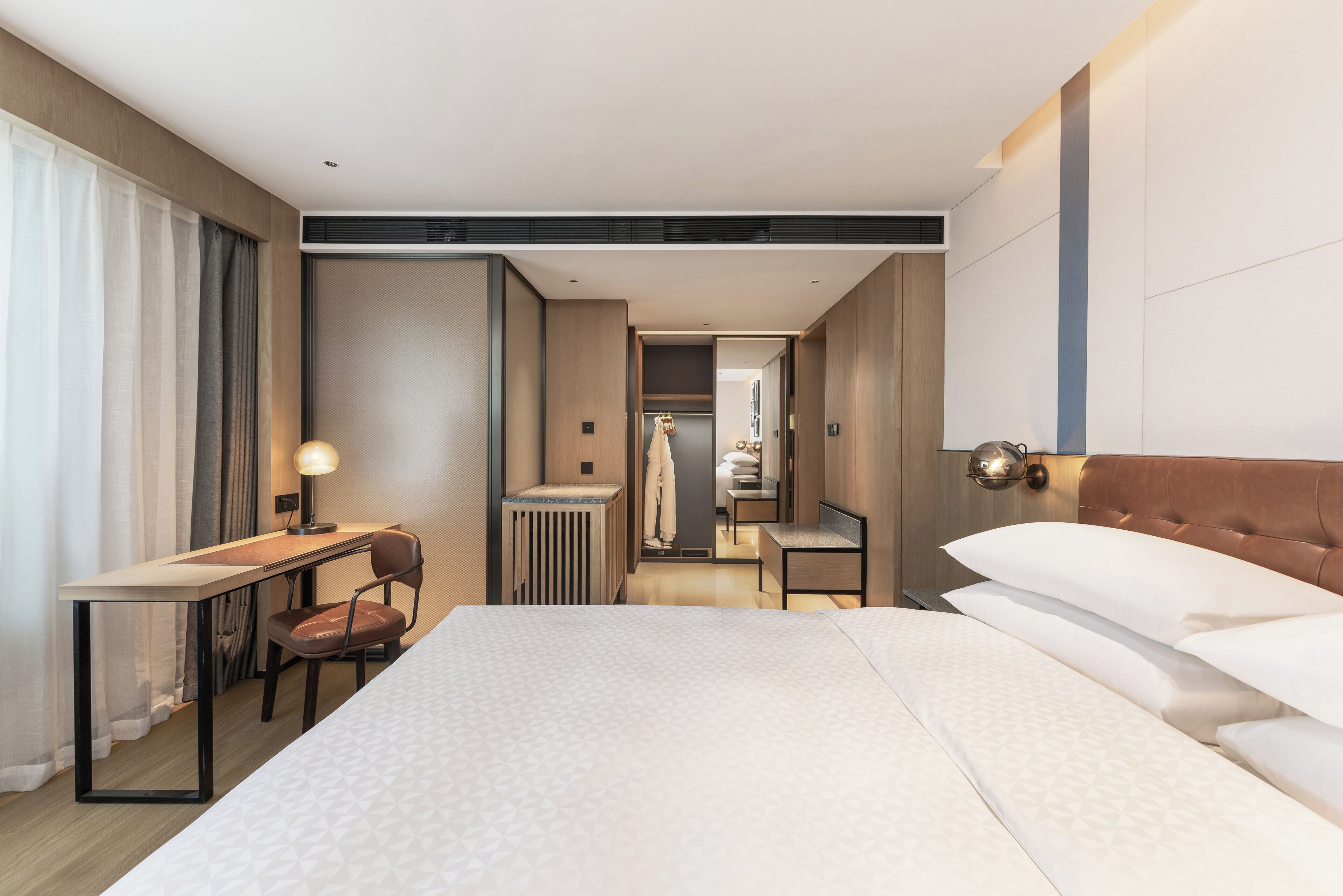 Quarto de hotel com uma cama grande, uma escrivaninha, uma cadeira, um espelho e um banheiro visível através de uma porta aberta.