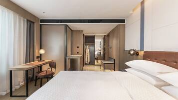 Quarto de hotel com uma cama grande, uma escrivaninha, uma cadeira, um espelho e um banheiro visível através de uma porta aberta.