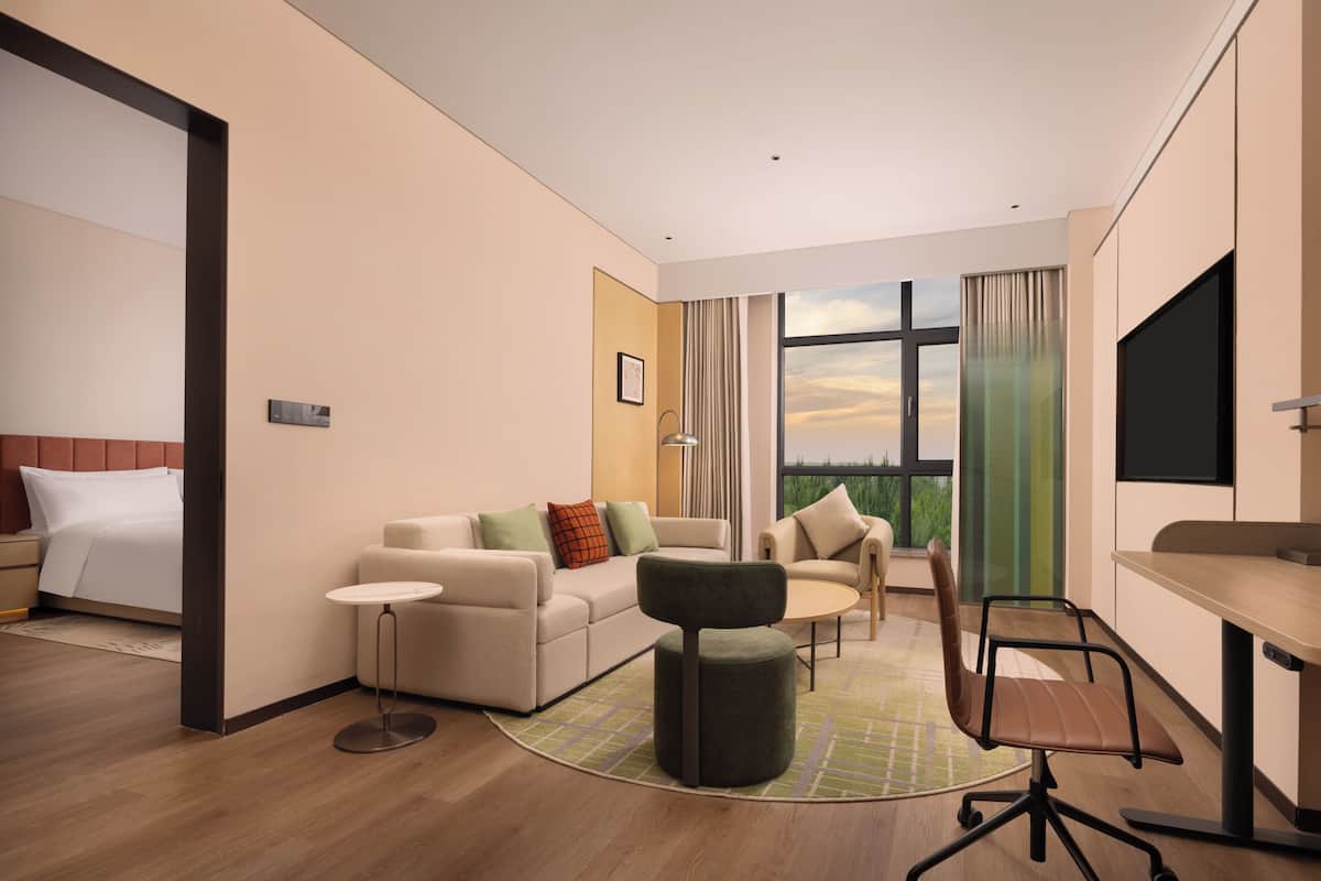 Quarto de hotel moderno com cama, sofá, escrivaninha e vista para o exterior.