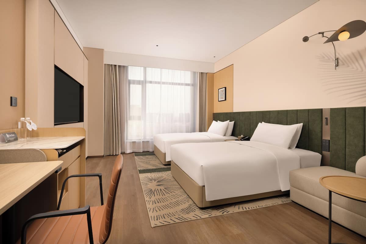 Quarto de hotel com escrivaninha, duas camas, sofá e televisão.