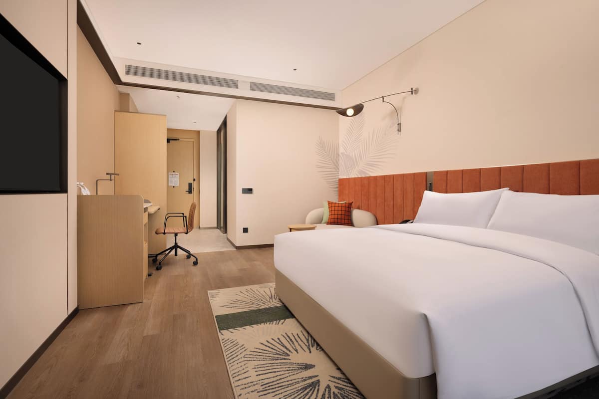 Quarto de hotel com cama, escrivaninha, cadeira e guarda-roupa.