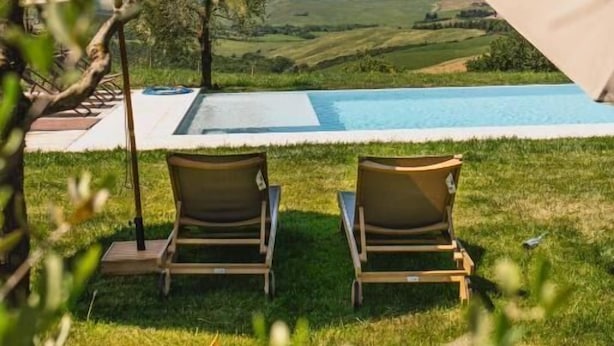 Área da piscina com duas espreguiçadeiras, um pérgola e vista para a piscina e paisagem.