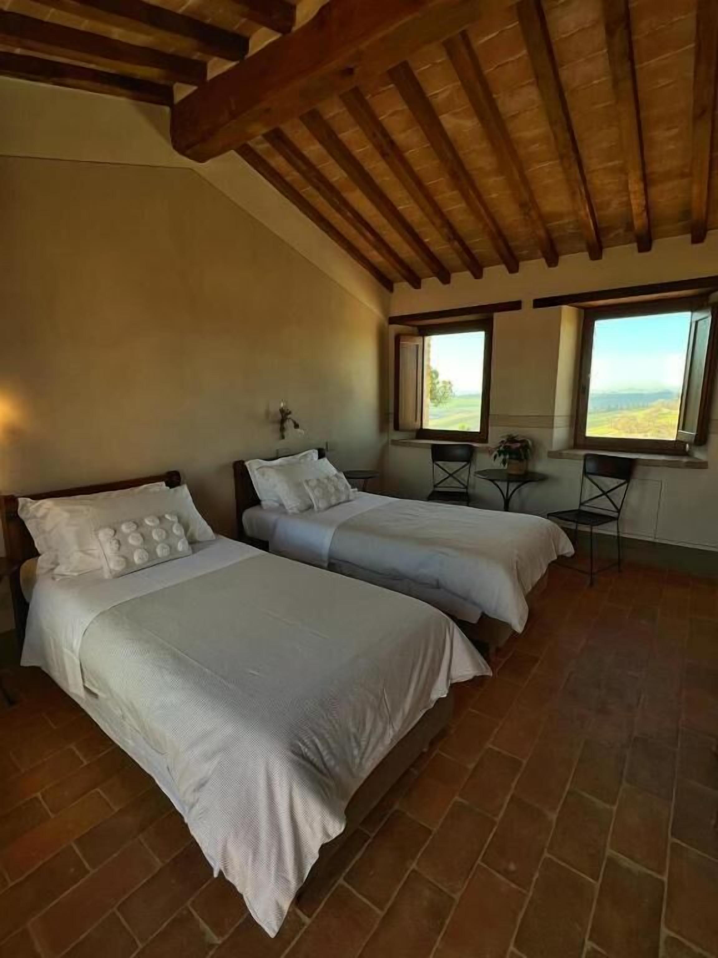 Quarto com duas camas, uma janela e vista para o campo.