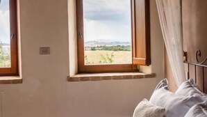 Quarto com cama, duas janelas e vista para o campo.