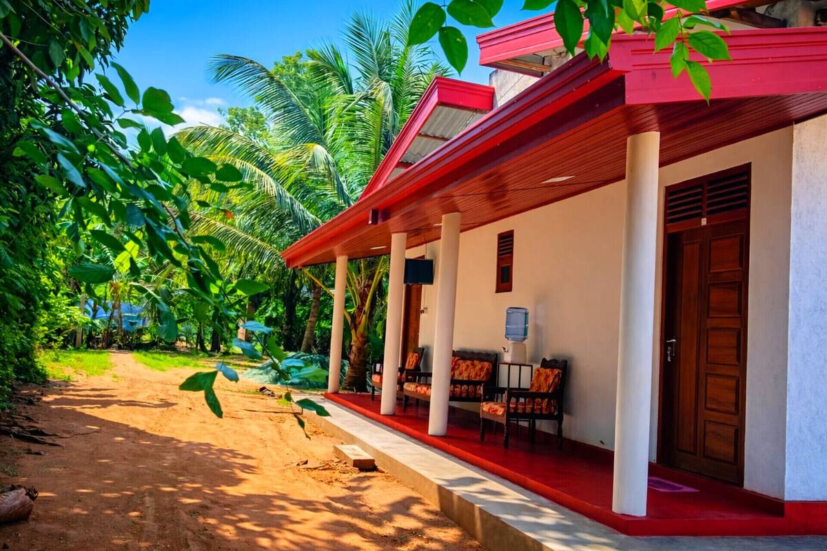 Uma casa com telhado vermelho e paredes brancas, cercada por vegetação exuberante.