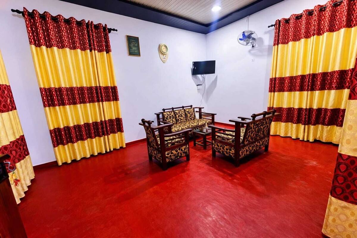 Quarto com piso vermelho, dois sofás, uma TV e cortinas com padrões vermelhos e amarelos.