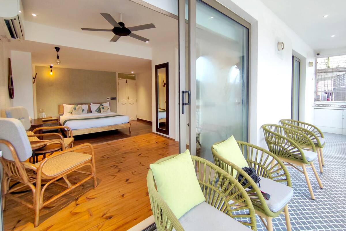Quarto de hotel moderno com cama, escrivaninha, cadeiras de vime e varanda com vista.