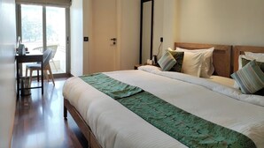 Quarto de hotel com uma cama grande, uma escrivaninha com cadeira, um espelho e vista através de uma porta.