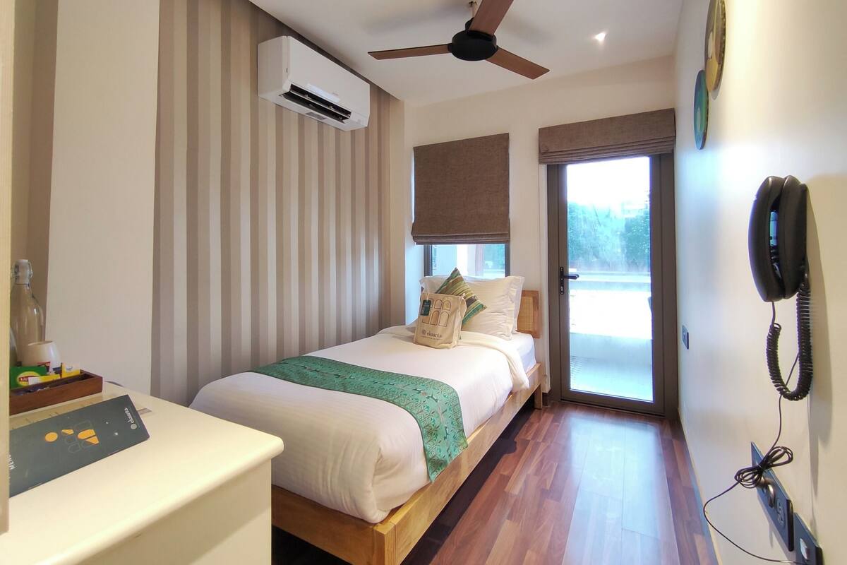 Quarto de hotel com cama, ar condicionado, ventoinha no teto, telefone ao lado da cama e vista pela porta.