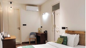 Quarto de hotel com cama, escrivaninha, cadeira e ar condicionado.