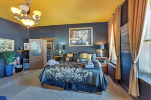 Quarto com uma cama grande, um candelabro, uma obra de arte emoldurada na parede e uma janela com cortinas.
