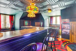 Uma área de bar com um balcão comprido, várias cadeiras, um lustre e um tapete colorido.