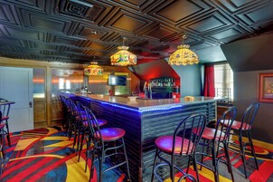 Uma área de bar com um balcão comprido, vários bancos e uma televisão.