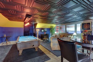 Uma sala com mesa de bilhar, dardos, sofá e mesa de jantar.