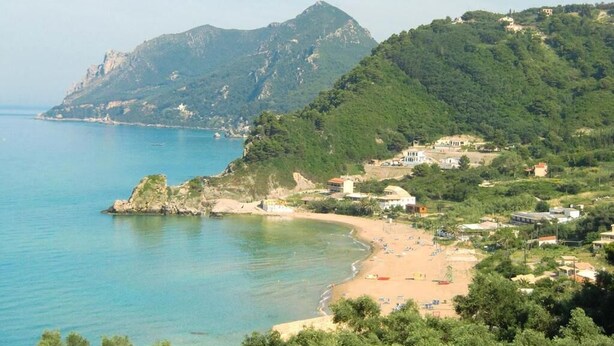 Paisagem costeira com praia, montanha e algumas construções espalhadas.