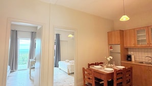 Ampla sala de estar com mesa de jantar posta para quatro, cozinha com armários de madeira e varanda com cortinas.