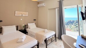 Quarto de hotel com duas camas, uma escrivaninha, uma cadeira, uma lâmpada no teto, ar condicionado e uma janela com vista.