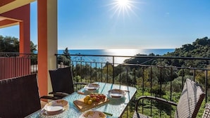 Uma varanda com mesa posta para refeição, com vista para a paisagem costeira.