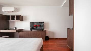 Quarto de hotel moderno com cama, escrivaninha, televisão exibindo o logotipo da Netflix, guarda-roupa e lixeira.