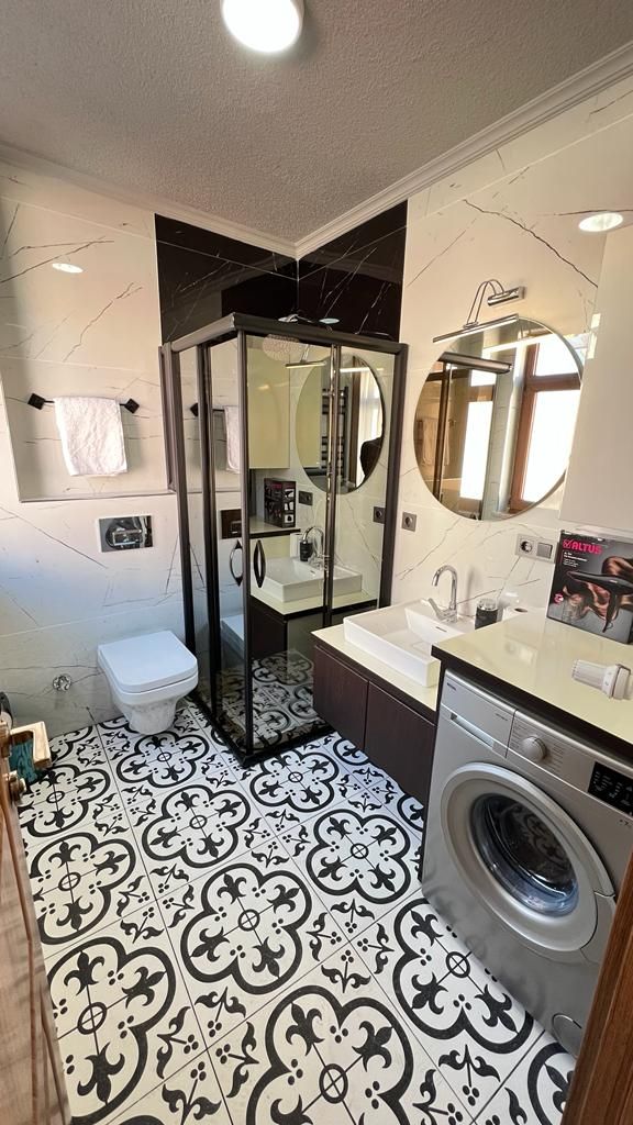 Casa de banho compacta com sanita, lavatório, espelho e máquina de lavar roupa.