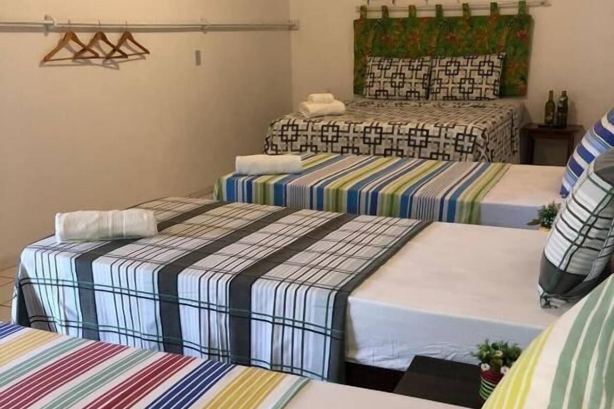 Quarto com três camas, cada uma com roupa de cama de diferentes estampas. Há uma televisão presa à parede acima das camas.