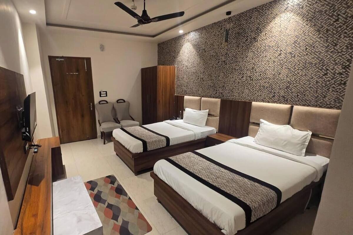 Quarto de hotel com duas camas, uma escrivaninha, um guarda-roupa e um ventilador de teto.
