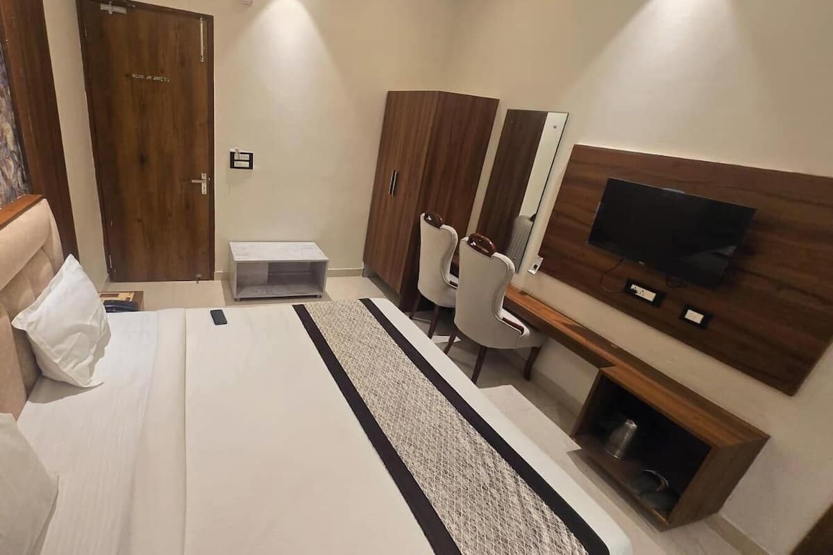 Quarto de hotel moderno com cama, escrivaninha, cadeira, televisão e guarda-roupa.