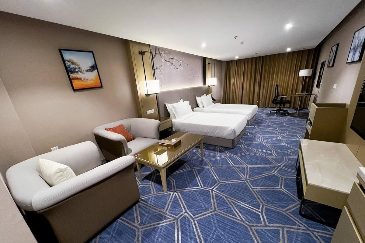 Quarto de hotel com duas camas, um sofá, uma mesa de centro e uma escrivaninha.