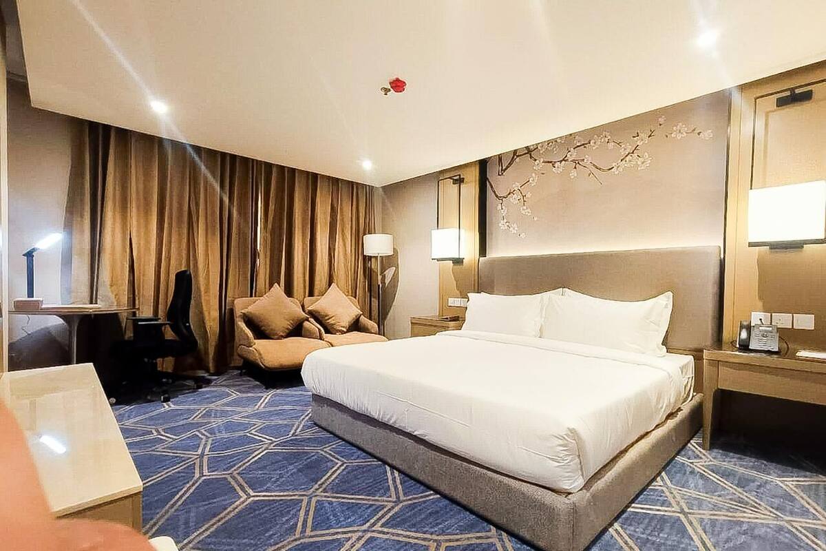 Quarto de hotel com uma cama grande, uma escrivaninha, uma cadeira e um carpete estampado.