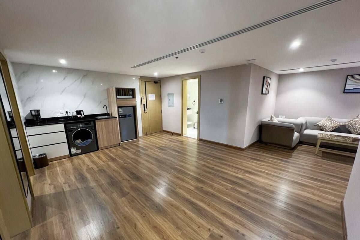 Ampla sala de estar com cozinha, piso de madeira e um sofá.