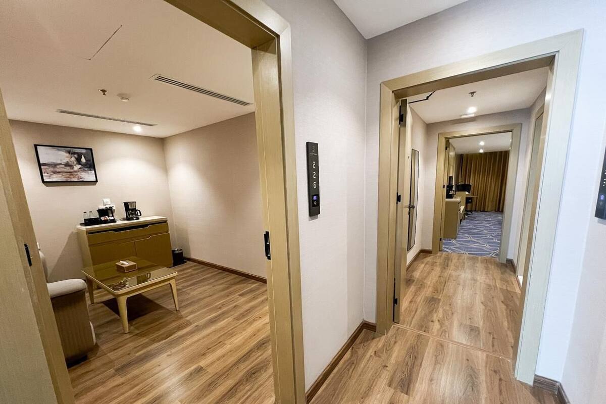 Um corredor de hotel com piso de madeira, uma mesa de vidro, um sofá bege e um pequeno armário.